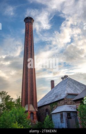 An orange brick smokestack set against a blue sky with an iron door and ...