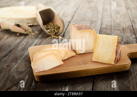 Block of yellow cheese with slices on wooden board with cherry tomatoes ...