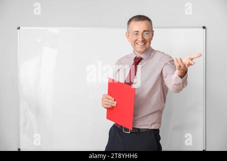 Male teacher with clipboard pointing at flipboard in classroom Stock ...