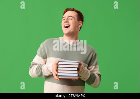 Emotional man holding stack of books on green background Stock Photo ...