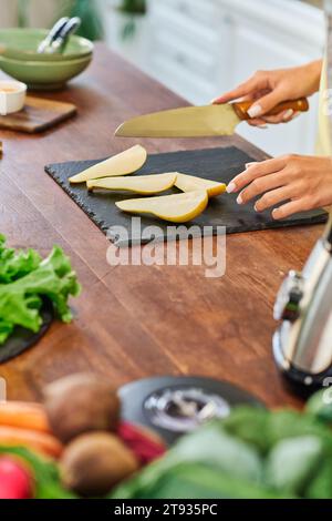 partial view of woman with knife near sliced cucumber on chopping board ...