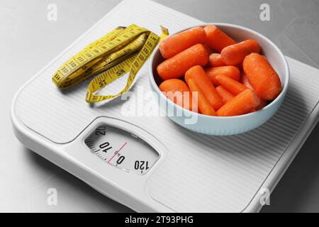 Healthy diet. Scale with carrots and measuring tape on light grey table ...