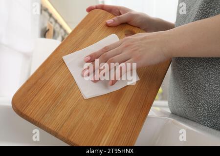 Woman wiping wooden cutting board with paper napkin at sink in kitchen ...