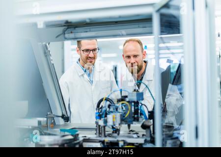 Colleagues in electronics factory watching machine work Stock Photo - Alamy