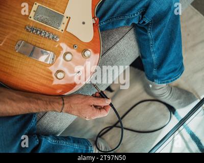 Person plugging cable into electric guitar while preparing for ...