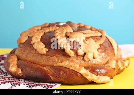 Rushnyk with korovai on yellow table against light blue background ...
