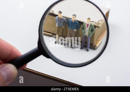 Tiny of men beside a book under magnifying glass Stock Photo - Alamy