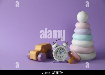 Alarm clock, toys and baby dummy on violet background. Time to give ...