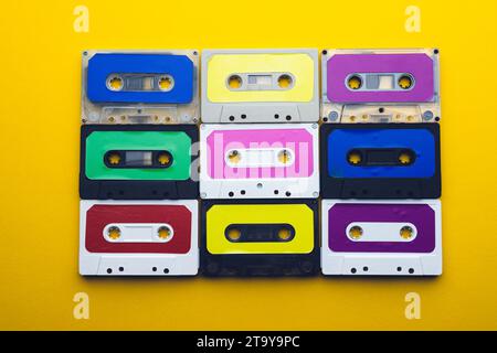 Overhead view of nine colourful cassette tapes arranged on yellow ...
