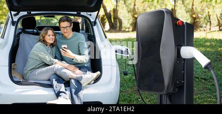 Loving couple with smartphones sits in an electric car's trunk Stock ...