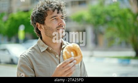 Young hispanic man eating doughnut and drinking coffee in shock face ...