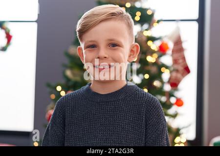 Adorable toddler smiling confident standing by christmas tree at home ...