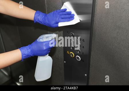 Woman wiping buttons of elevator`s panel with detergent and paper ...