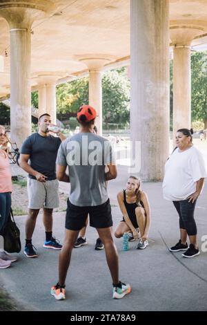 Rear view of male fitness coach and kids performing sit ups at a ...