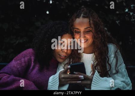 Curious teenage girl sharing smart phone with male and female friend at ...