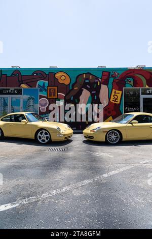 Brightly colored Porsche sports cars parked near a mural in an arts ...