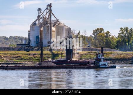 Tugboat pushing freight barges past grain loading dock in farming ...
