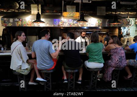 Customers having lunch by a open kitchen in a grill restaurant inside ...