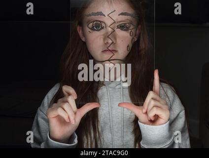 Teenage girl holds a tranparent perspex sheet with drawing of half a ...