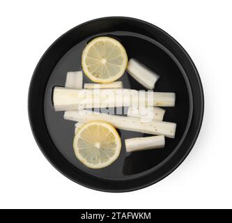 Bowl with water, lemon and raw salsify roots on white table, closeup ...