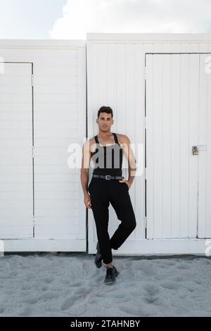 handsome young cuban man in black attire posing with hands in pockets ...