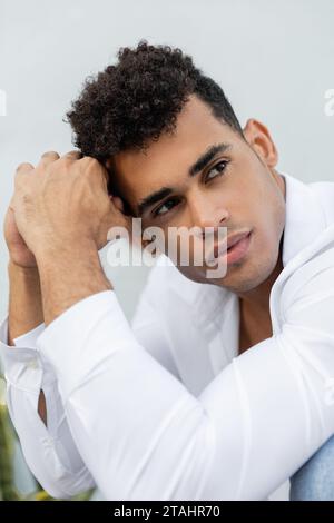Trendy young cuban man posing near white wall with shadow on urban ...