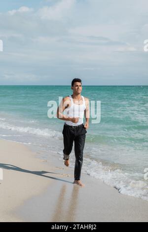 Smiling and muscular young cuban man having fun while standing in ocean ...