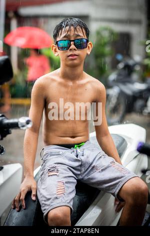 A cool little Filipino boy strikes a cool pose with his shades on in the rain in Tondo, Manila ...
