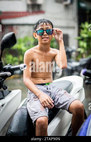 A cool little Filipino boy strikes a cool pose with his shades on in the rain in Tondo, Manila ...