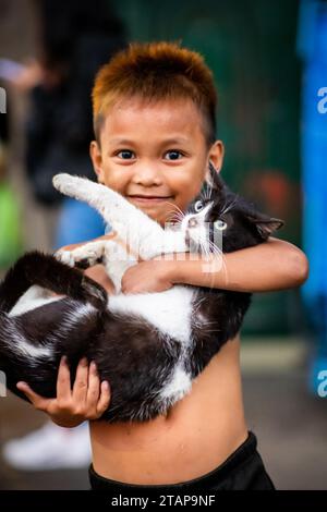 A cute young filipino boy holds his pet cat in Manila, The Philippines ...