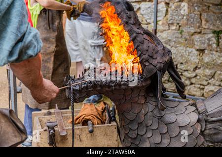 Demonstration of blacksmithing in a dragon head shaped forge during medieval festival in ...