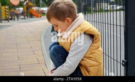 Little boy crying next to metal fence on public playground. Child ...