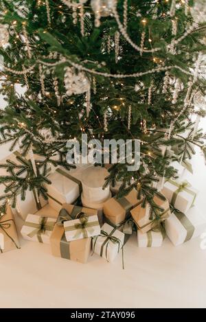 Many gift boxes under Christmas tree indoors, closeup. Space for text ...