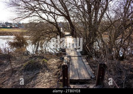 An old damaged pedestrian bridge in a village, spanning a river and ...