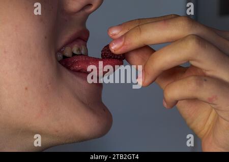 teenage girl puts red raspberries on her tongue with her fingers to eat ...