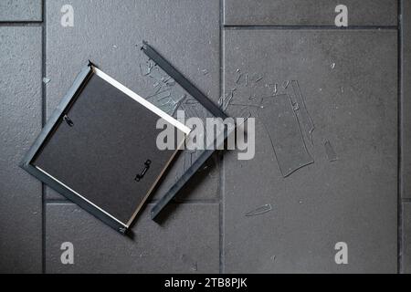 A broken picture frame on a tiled floor, with the frame itself broken ...