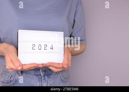 Female hands hold lightbox with 2024 numbers in front of yellow ...