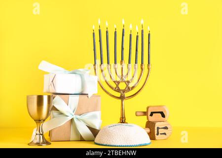 Menorah with Torah, gift boxes, dreidels and cup on yellow background ...
