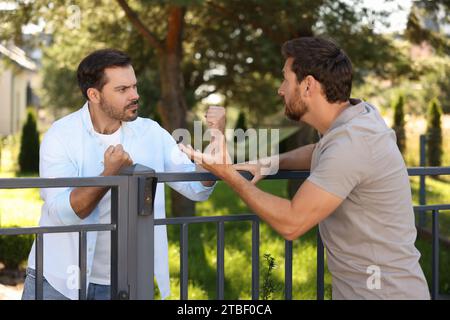 Angry neighbours having argument near fence outdoors Stock Photo - Alamy
