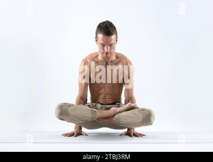 advanced male yogi doing tolasana (scale pose) on a white mat with a ...