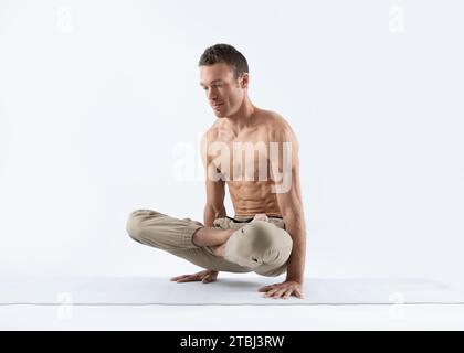 advanced male yogi doing tolasana (scale pose) on a white mat with a ...