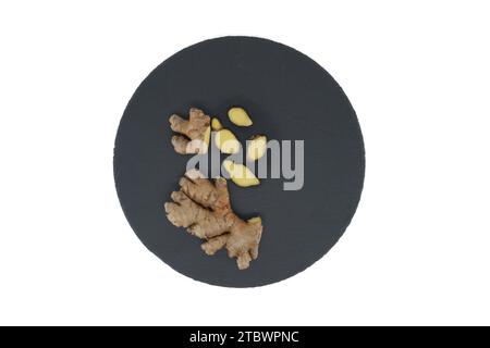 Ginger rhizome with slices on round stone slate coaster. Top view with ...