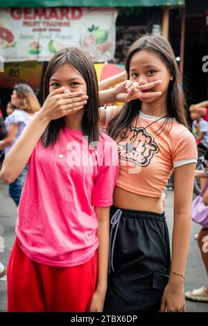 Two young Filipino girls make a cheeky pose and hand signal during a ...