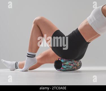 Faceless woman doing roller exercise for myofascial release on white ...