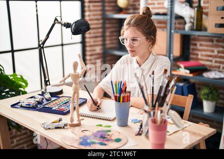 Young woman sitting by manikin at small business hugging oneself happy ...