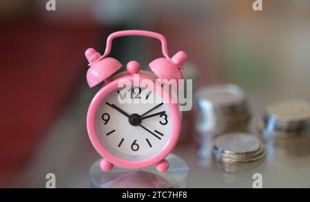 Pink alarm clock compass and stacks of coins closeup Stock Photo - Alamy
