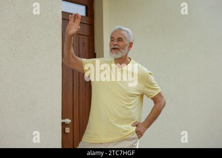 Neighbor greeting. Happy senior man waving near fence outdoors Stock ...