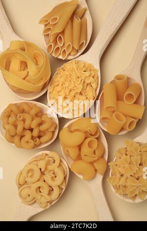 Spoons with different types of uncooked pasta on wooden background ...