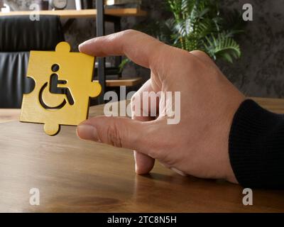 A hand holds puzzle disabled person symbol in the workplace as a symbol ...