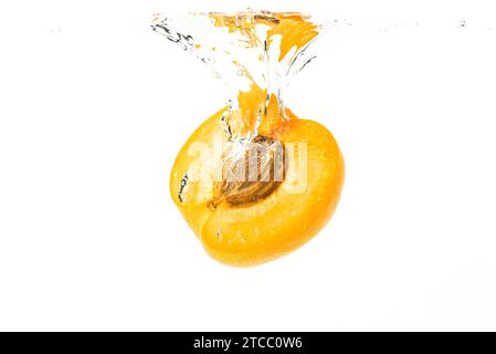 Fresh ripe organic apricot split in half falling in the clear water ...
